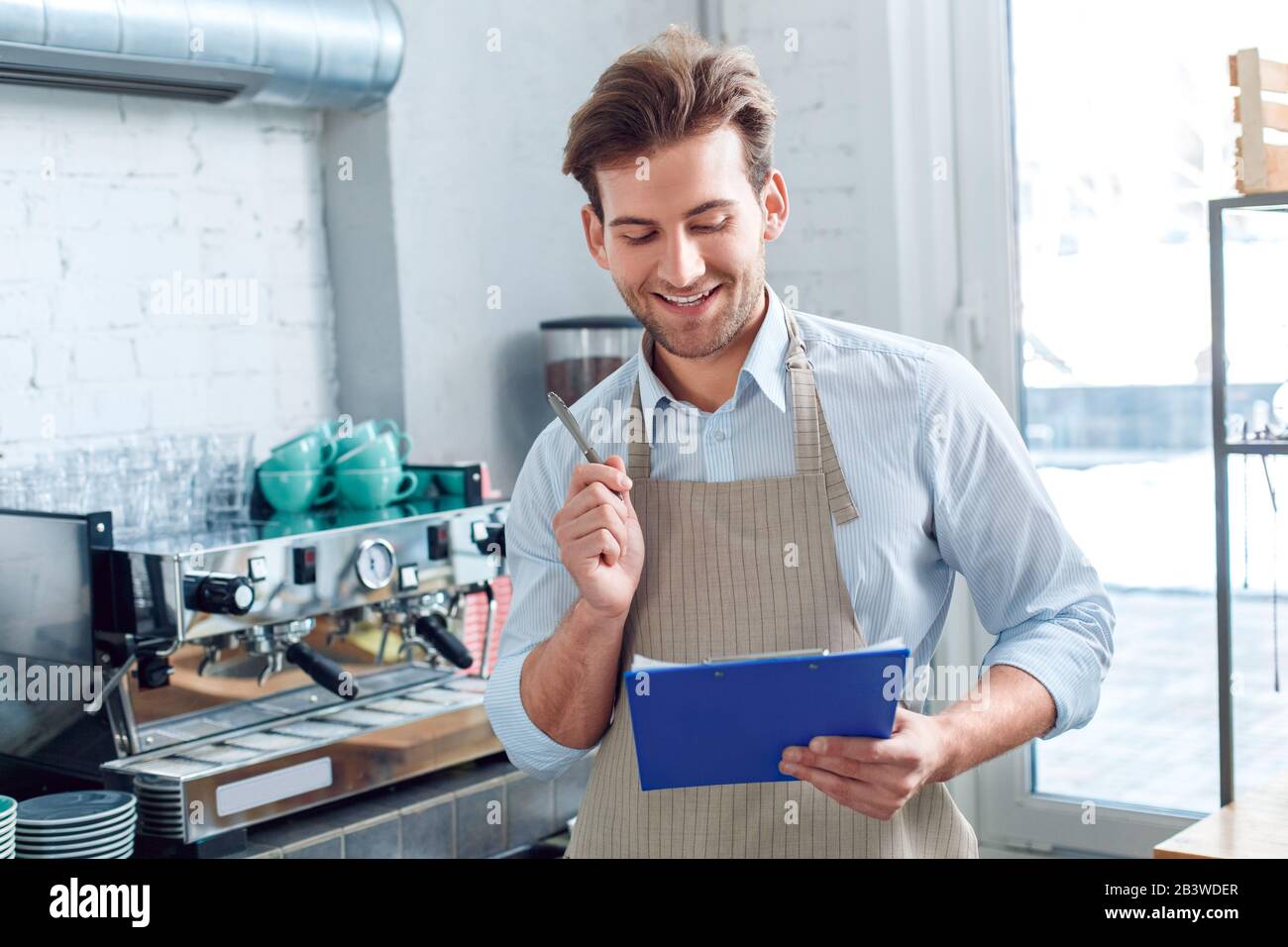 Young adult barista working in coffeeshop, making important notes in ...