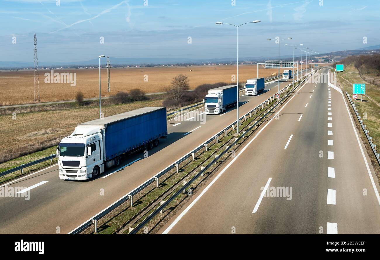 Convoy of transportation trucks passing on a highway on a bright blue ...