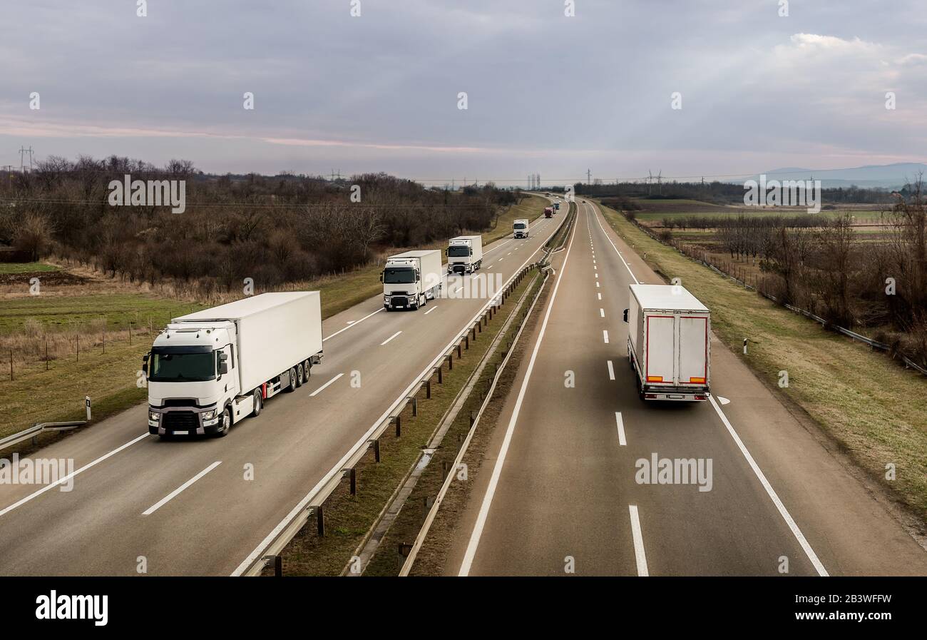 Convoy of transportation trucks passing on a highway on a bright blue ...