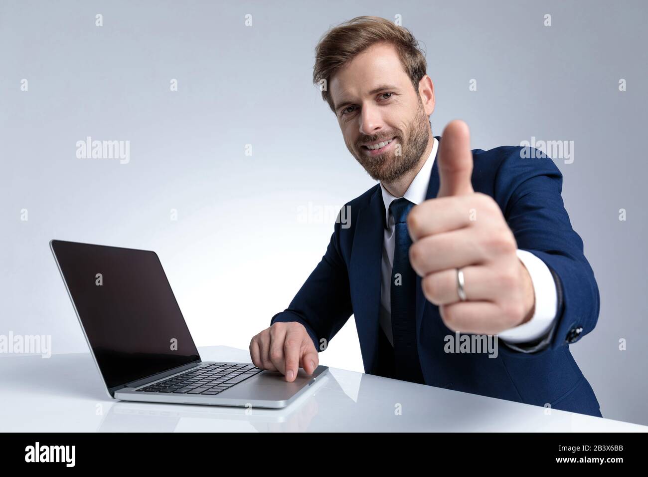 Cheerful businessman giving a thumbs up and working on his laptop while ...