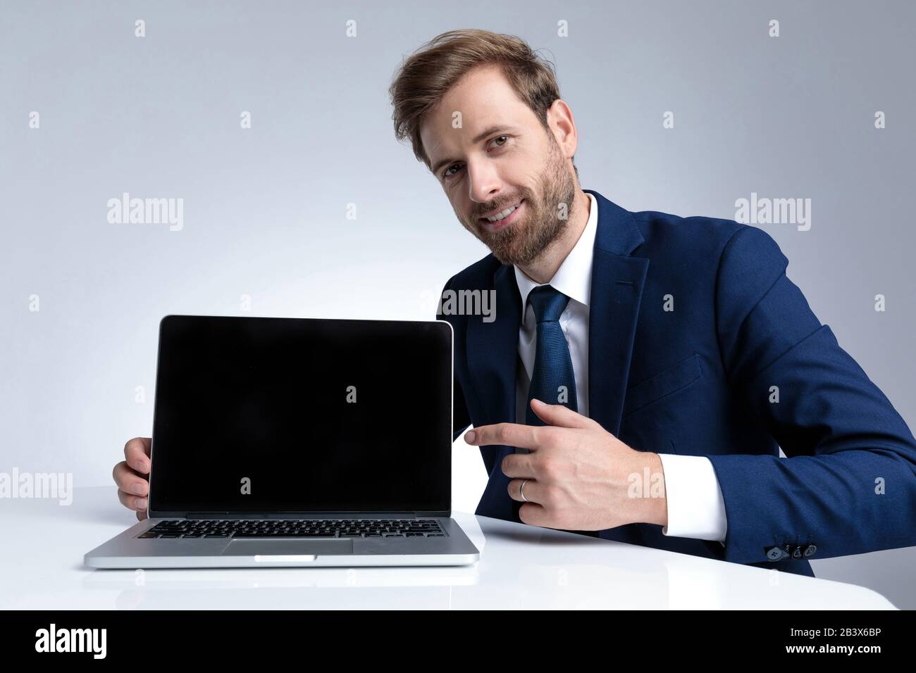Confident businessman pointing to his laptop and smiling while wearing ...