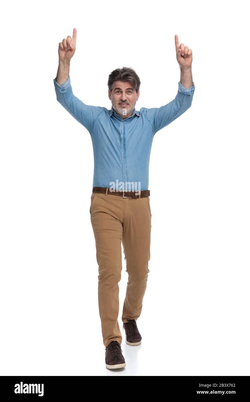 Cheerful casual man pointing up with both hands while walking on white ...