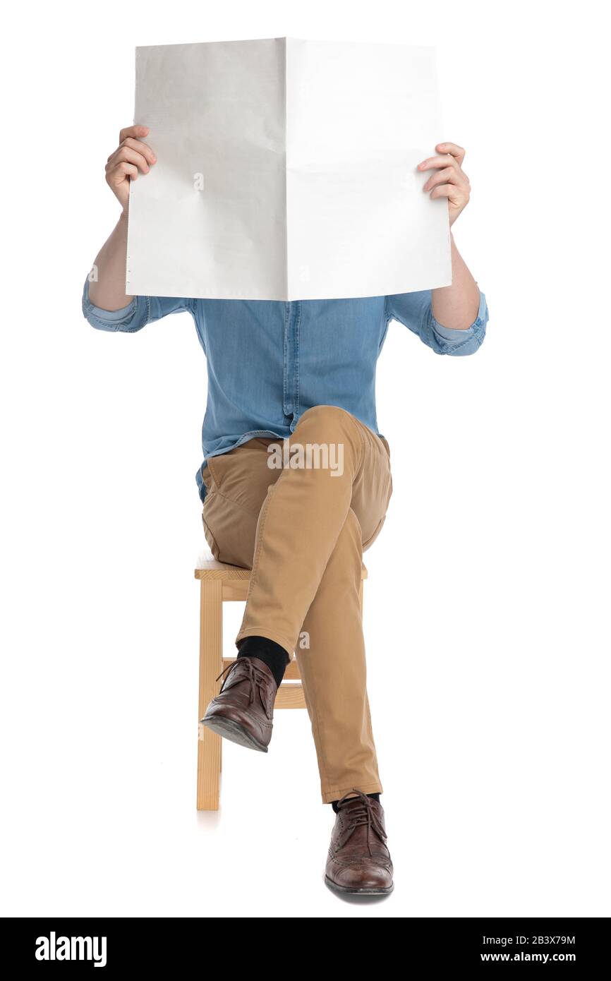 young casual man hiding behind newspaper and sitting isolated on white ...