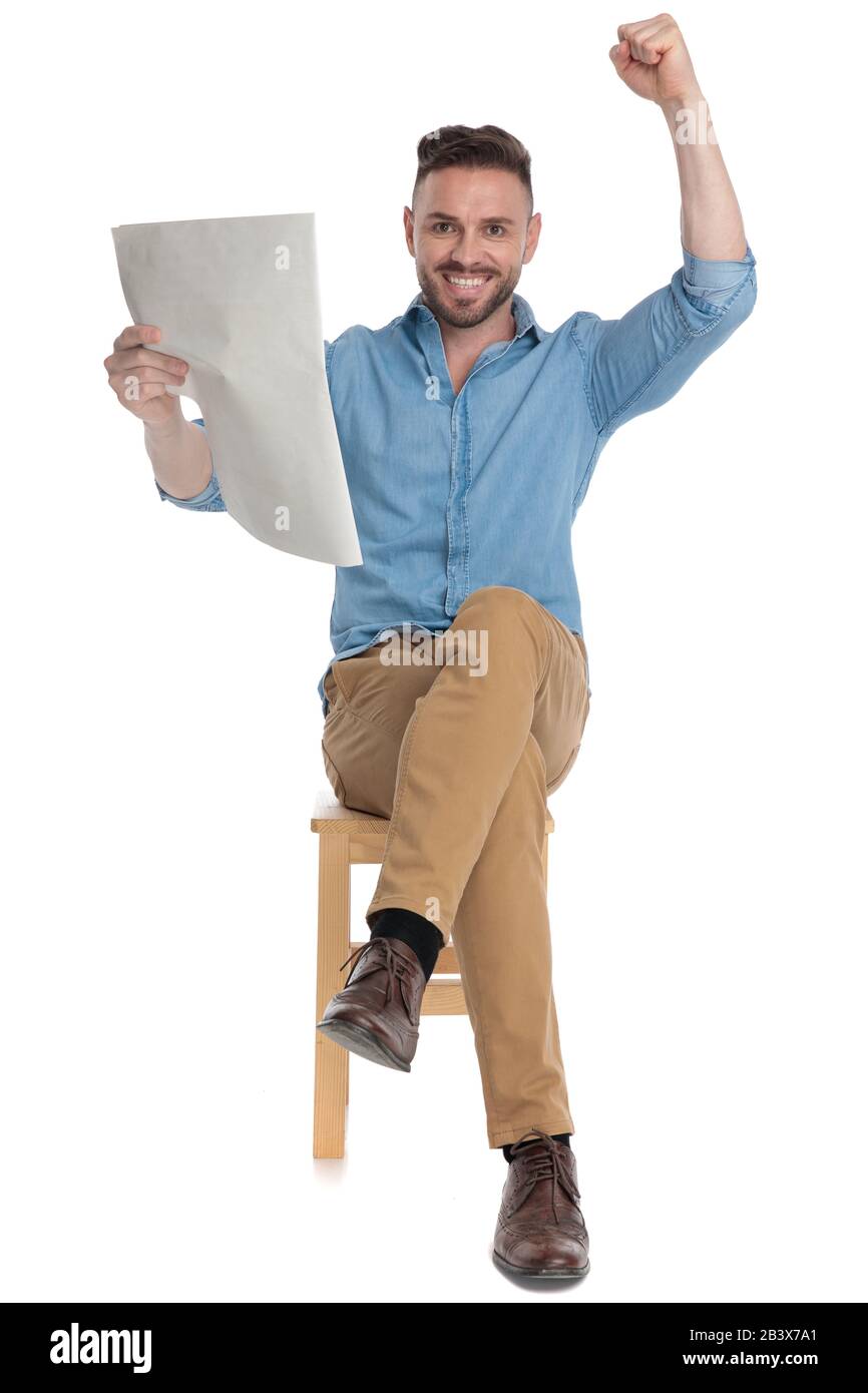 happy young man holding newspaper and celebrating victory, sitting ...