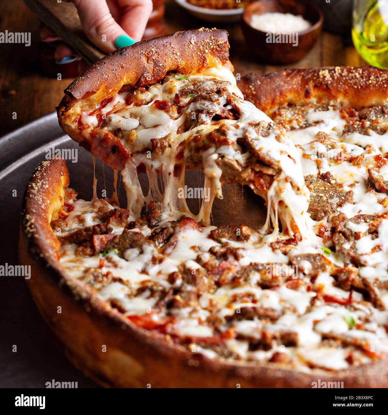 Deep dish meat pizza on a wooden table with a slice being pulled Stock ...