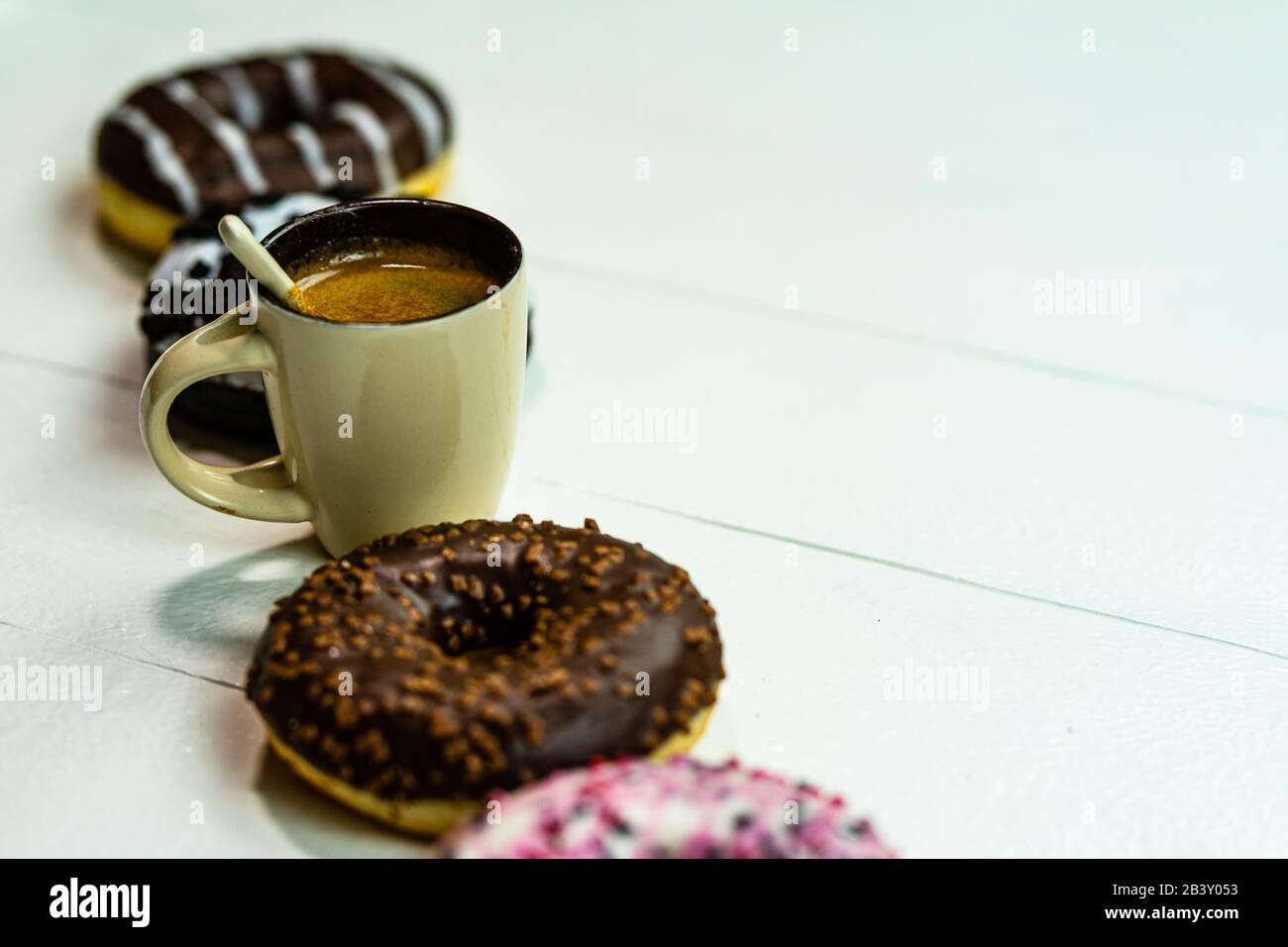 Colorful donuts and coffee cup on white wooden table. Sweet bakery with ...