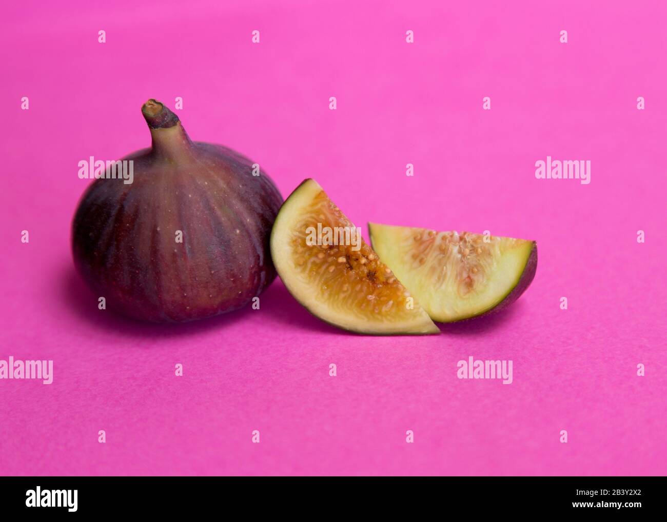 Two figs, one whole and one cut, lie on a bright pink background Stock ...