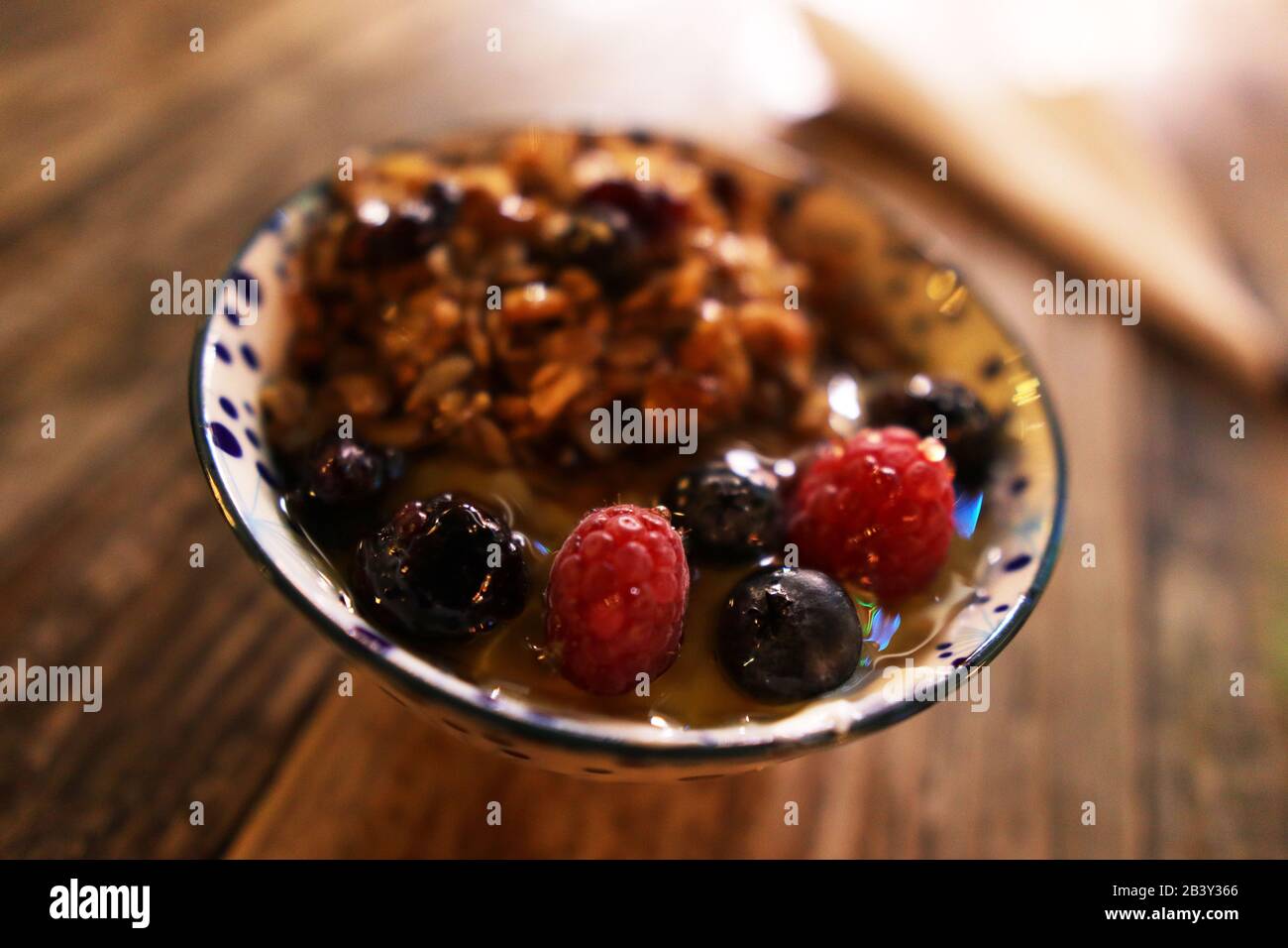 Raspberry, blueberry, and granola cereal bowl on rustic wood tabletop ...