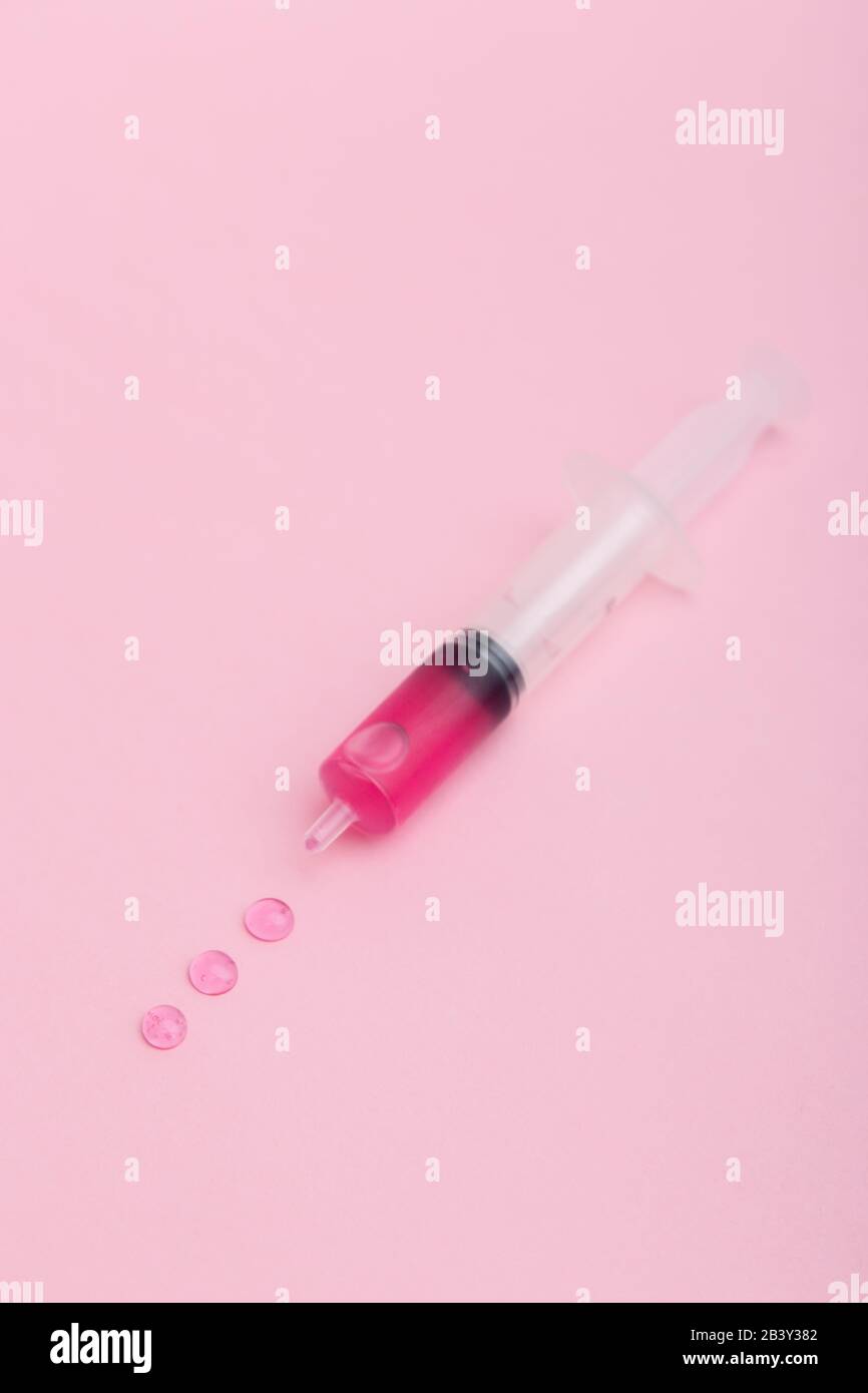 A syringe with pink liquid is half filled and lies on a pink background ...