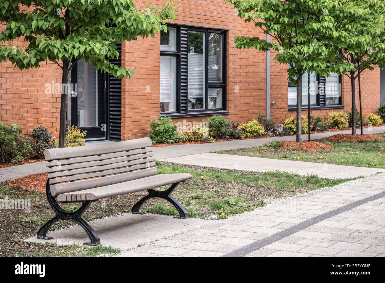 Bench in front of a modern brick building. Green city neighborhood in ...
