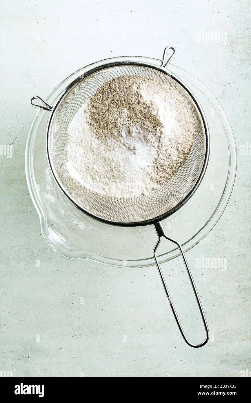 sifting flour through a sieve into a large glass bowl Stock Photo - Alamy
