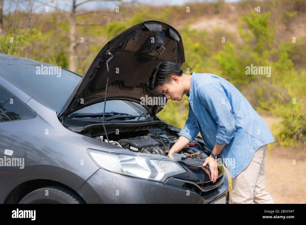 Asian young unhappy man inspecting broken car engine in front of the ...