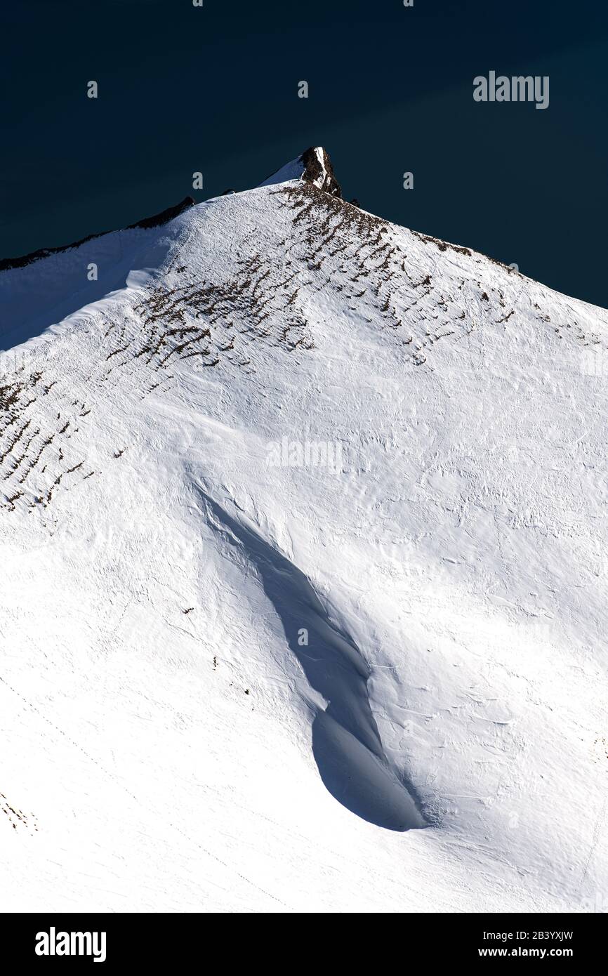 Snowdrift and snow hole with a pointed peak with lake in the background ...