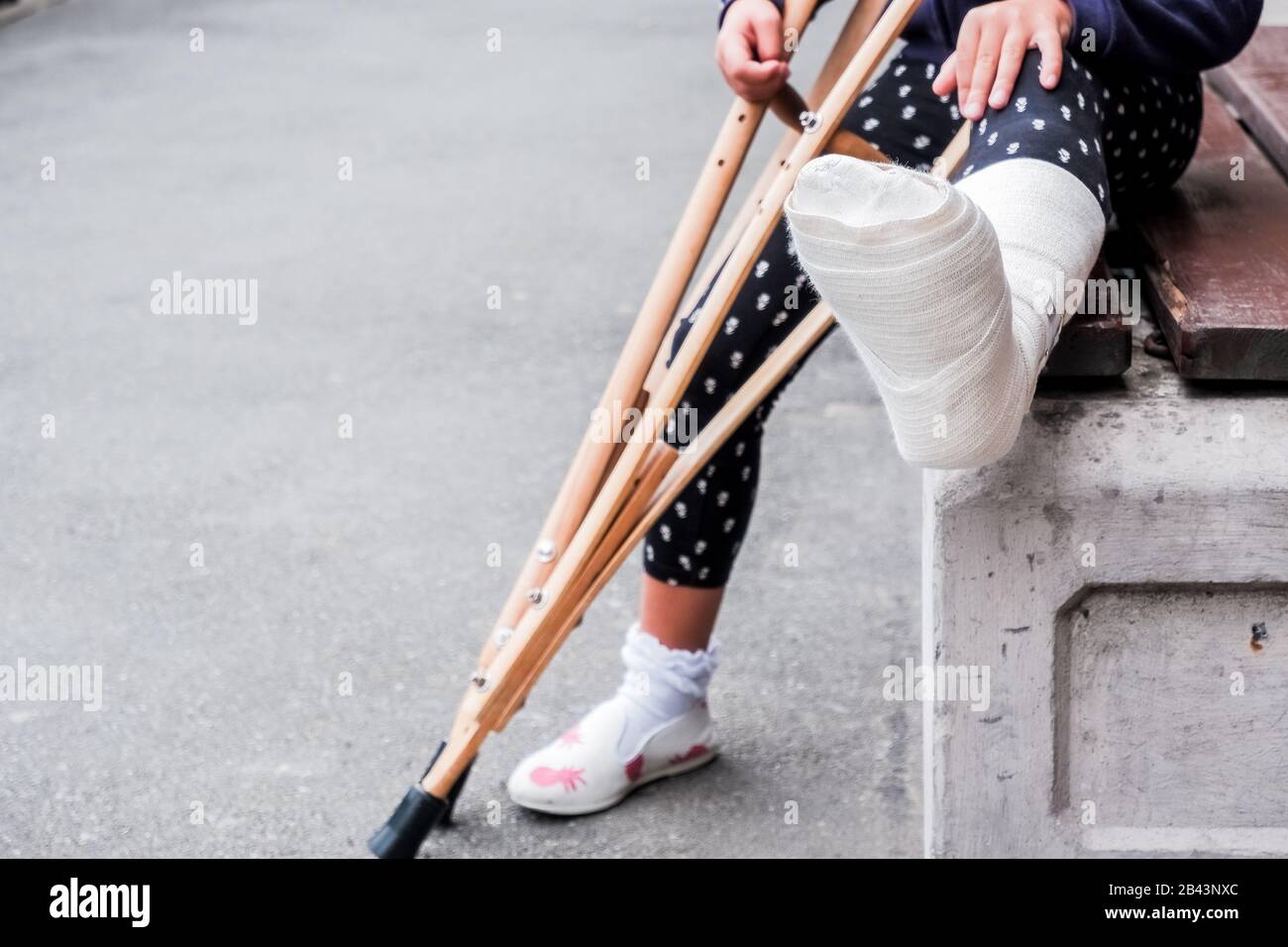 unrecognizable girl sits on the street on a bench with a broken leg and ...