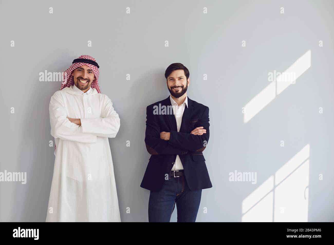 Arab and european businessmen stand smiling at the gray background ...