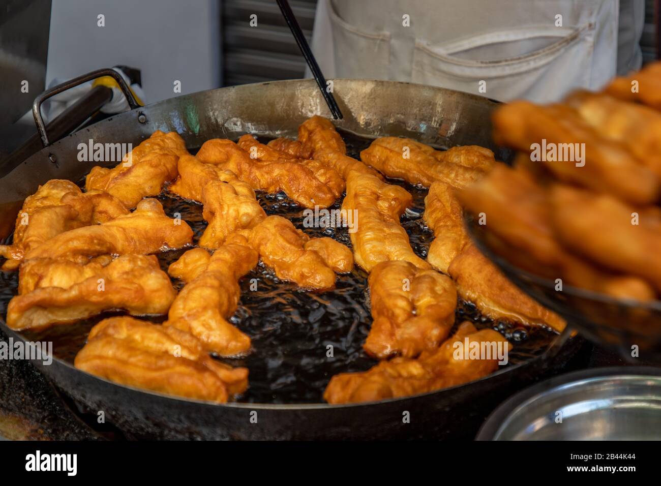 Chinese deep fried dough in hot oil on steel pan. Youtiao, Padnoongo or ...