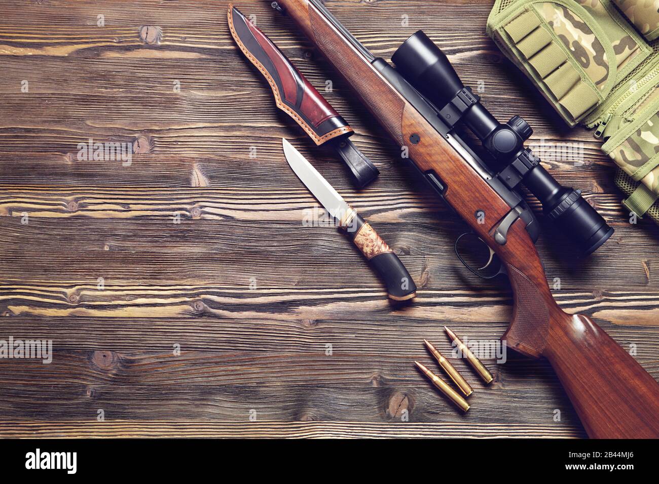 A gun with an optical sight, a hunting knife on a wooden background.Top ...