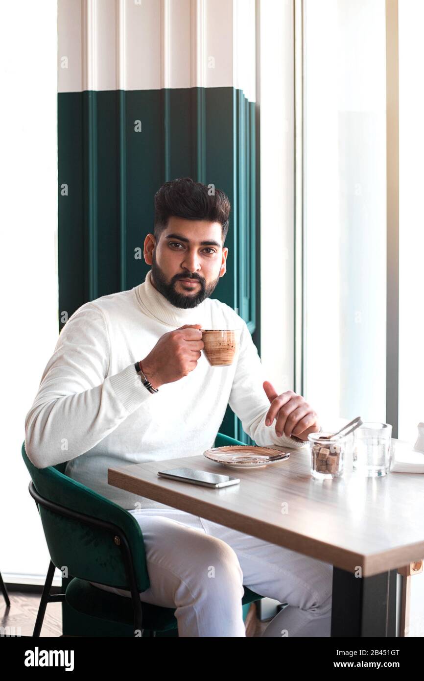 Young indian man drinking coffee in cafe and looking at camera Stock ...
