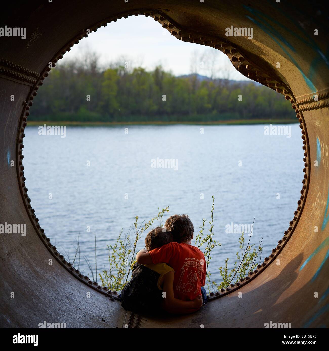 Two young brothers sit together and embrace inside empty rusty drain ...
