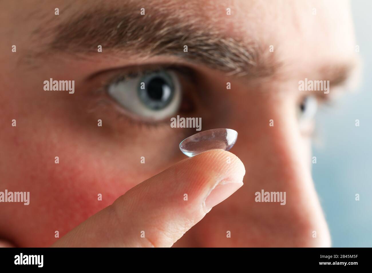 Inserting a corrective contact lens. Man with blue eyes Stock Photo - Alamy