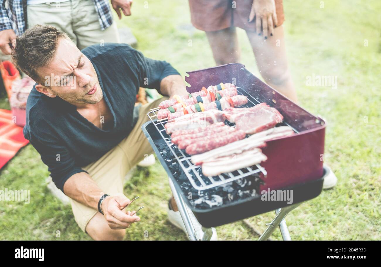 Millennial man blowing on barbecue fire at backyard outdoor dinner ...