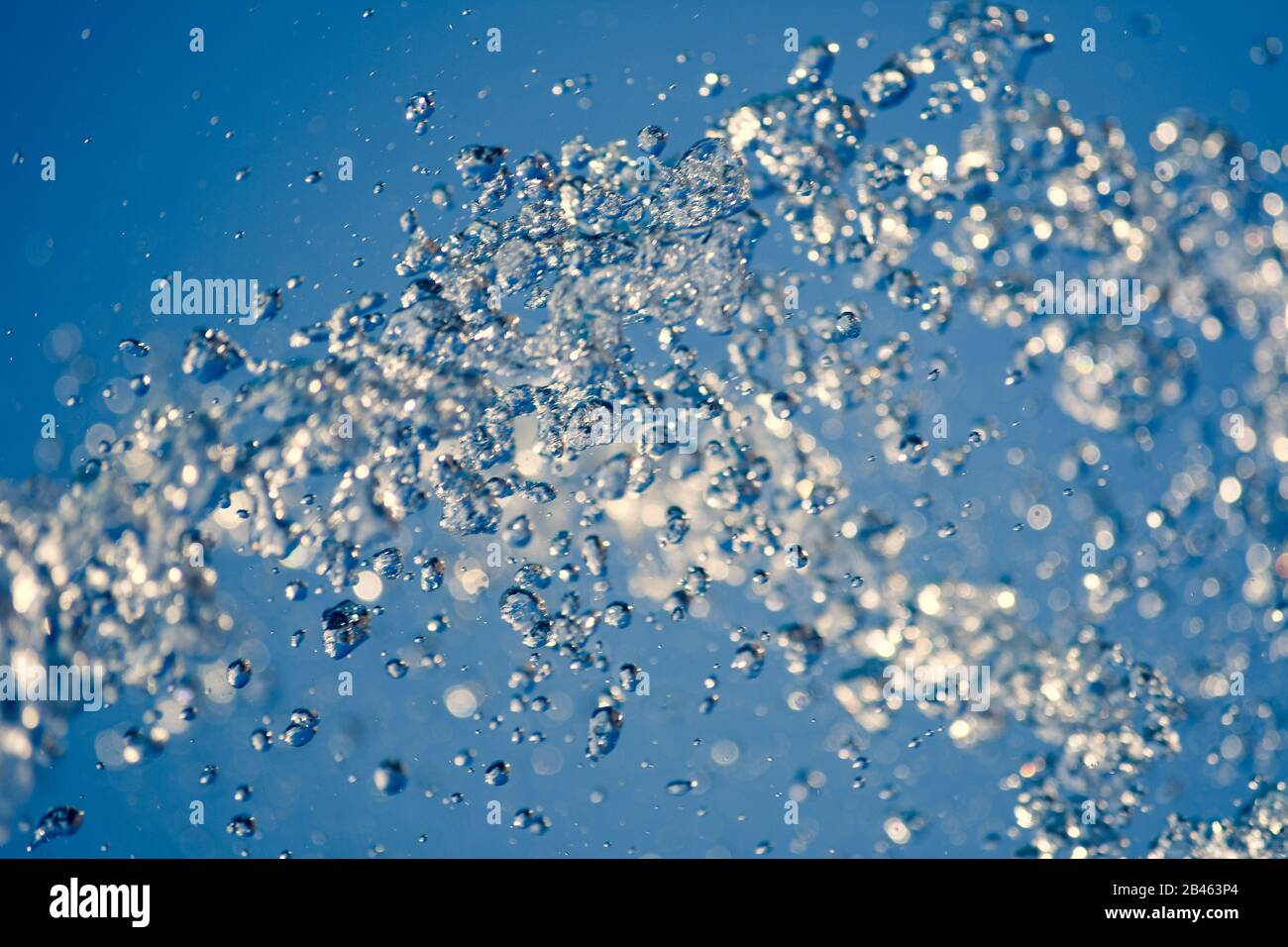 Water droplets spraying from a fountain in abstract design on blue sky ...