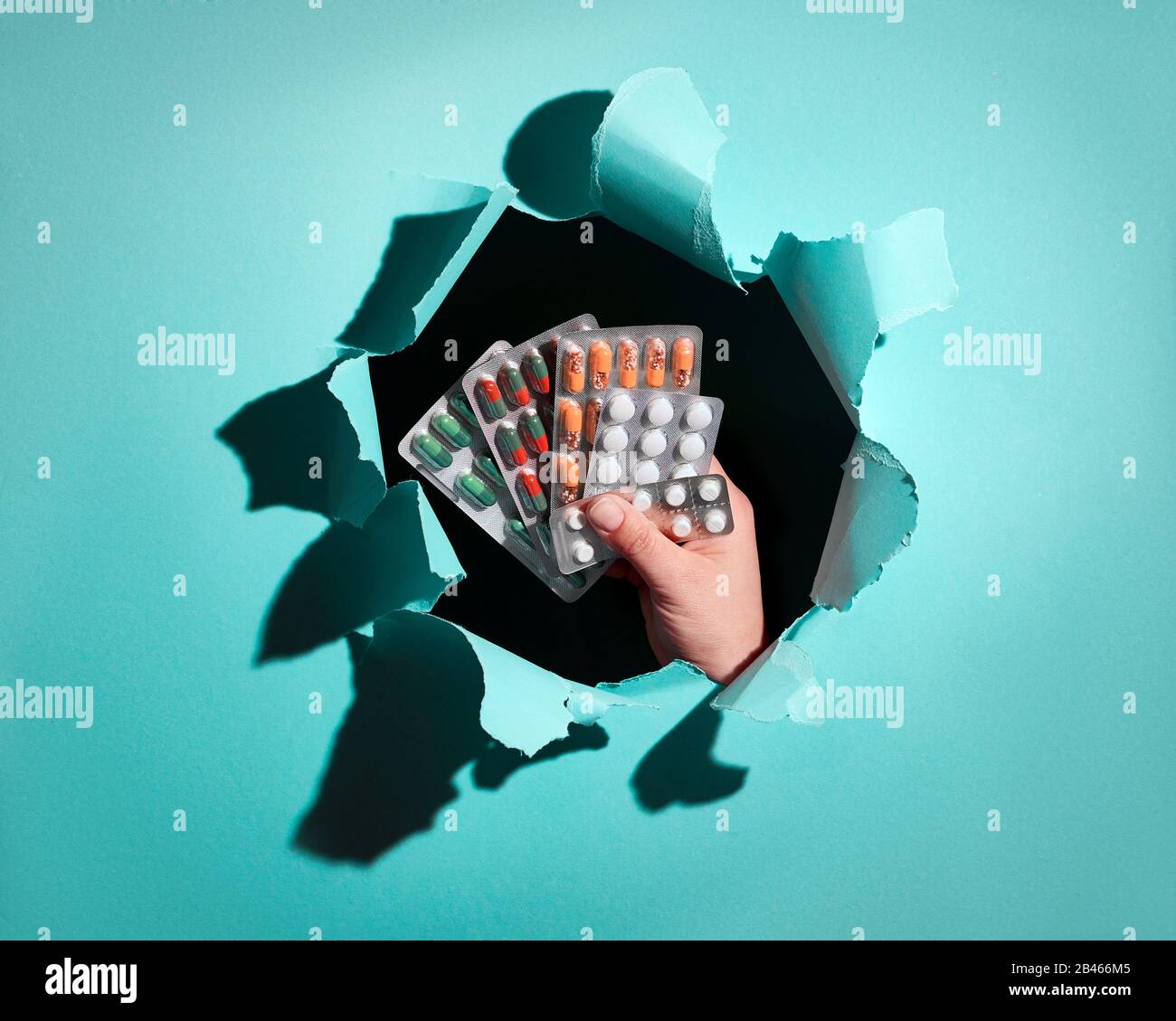 Assorted pills or capsules with medicines in hand framed by paper hole ...
