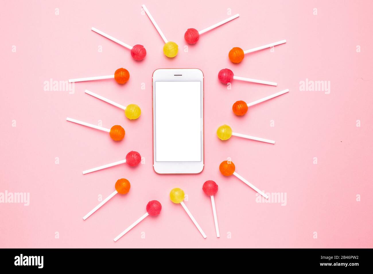 Mobile phone with pink and yellow candy on a pastel pink background top ...