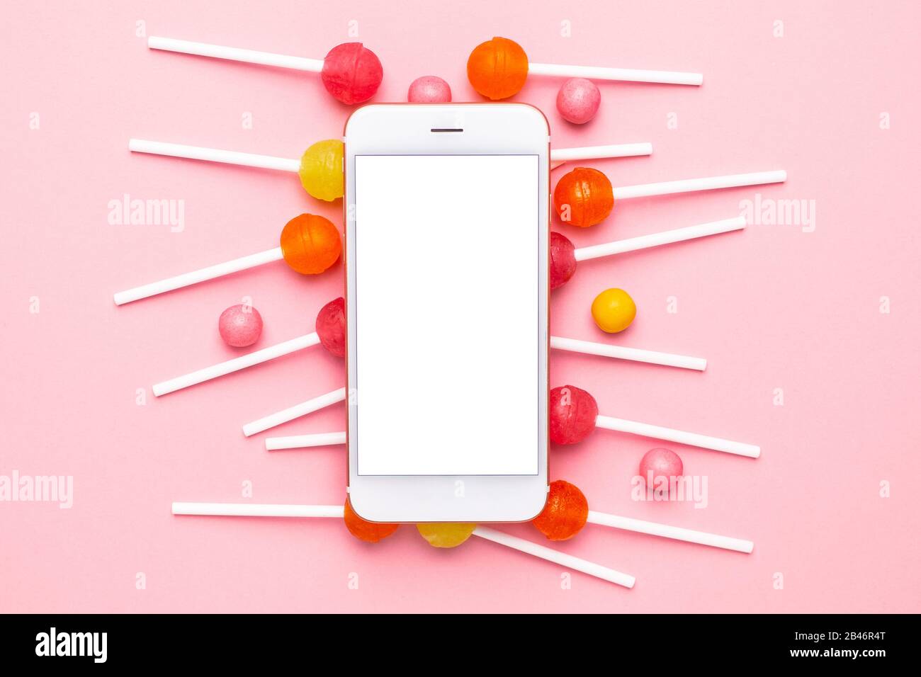 Mobile phone with pink and yellow candy on a pastel pink background top ...