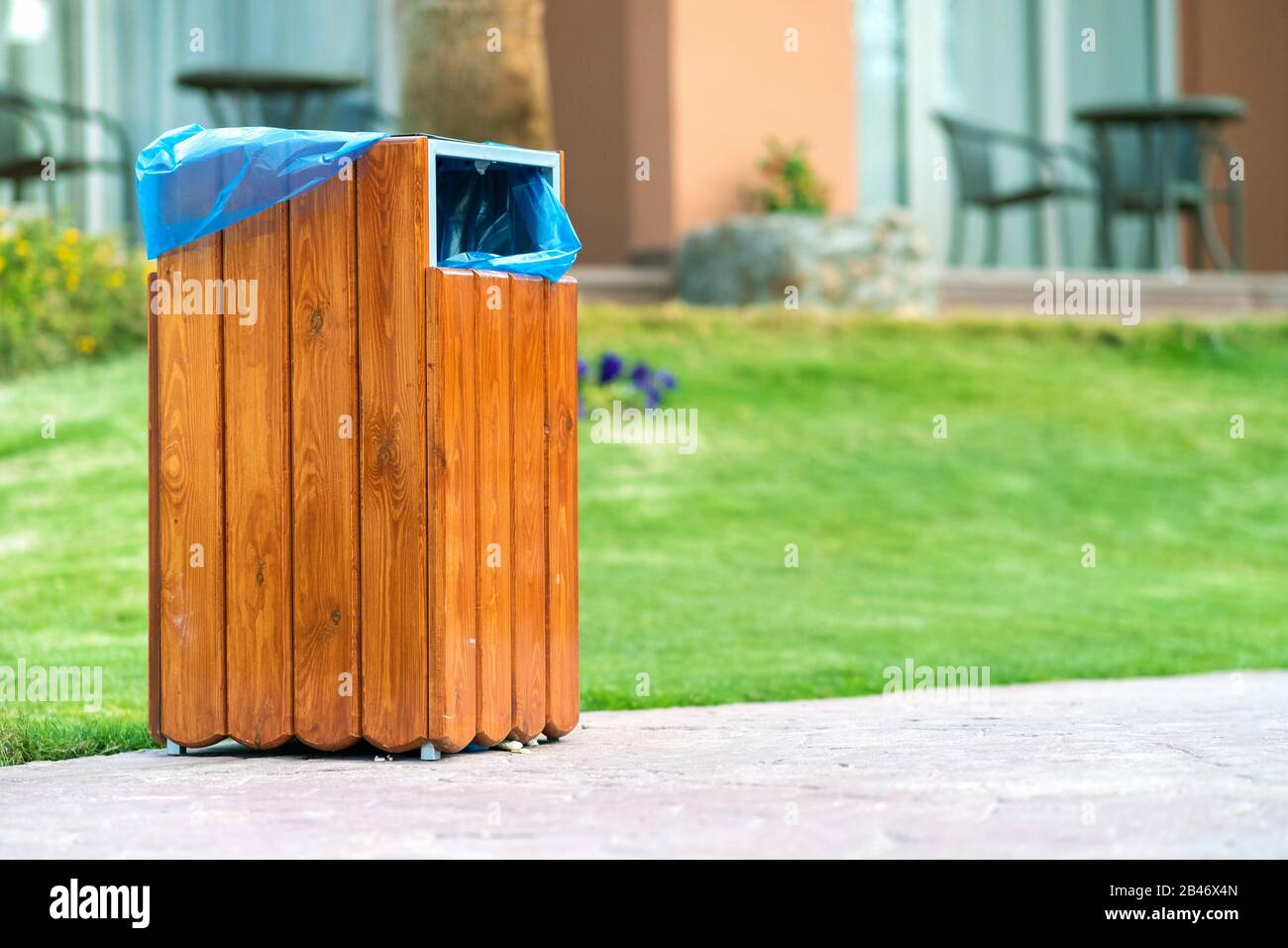 Yellow wooden trash can outdoors on the side of sidewalk in park ...