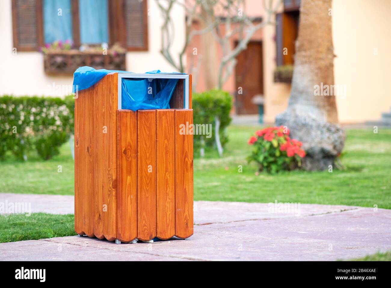Yellow wooden trash can outdoors on the side of sidewalk in park ...