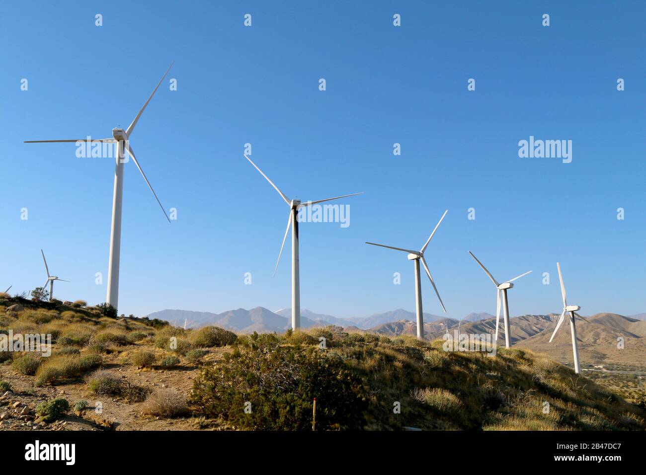 a beautiful desert mountain crest with a row of wind farm turbines ...