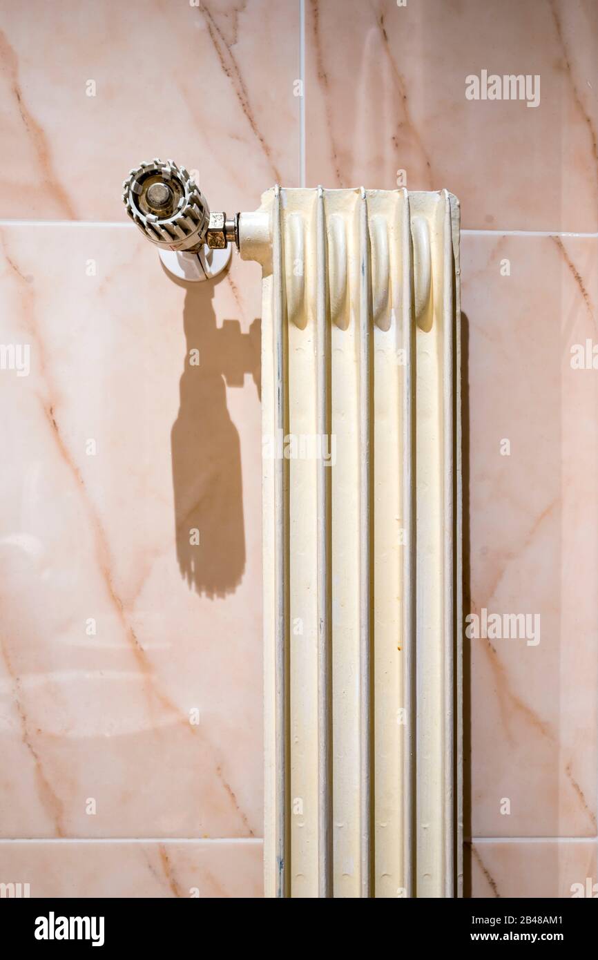 narrow home heating radiator with regulator close to tiled wall Stock ...