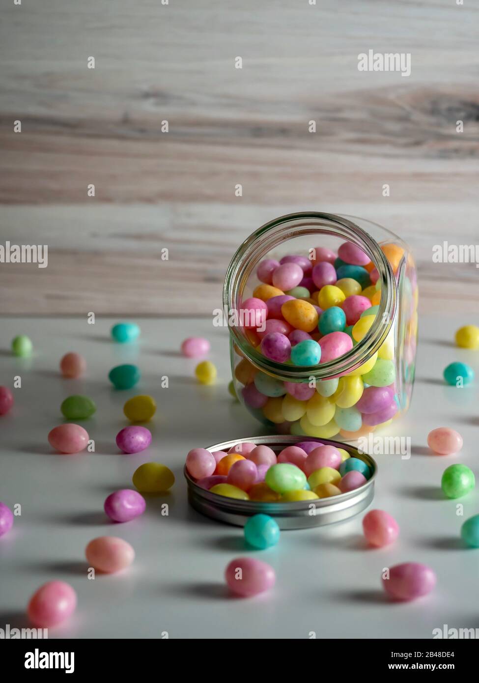 Pastel colored jelly beans in a glass jar spilling out onto a white ...