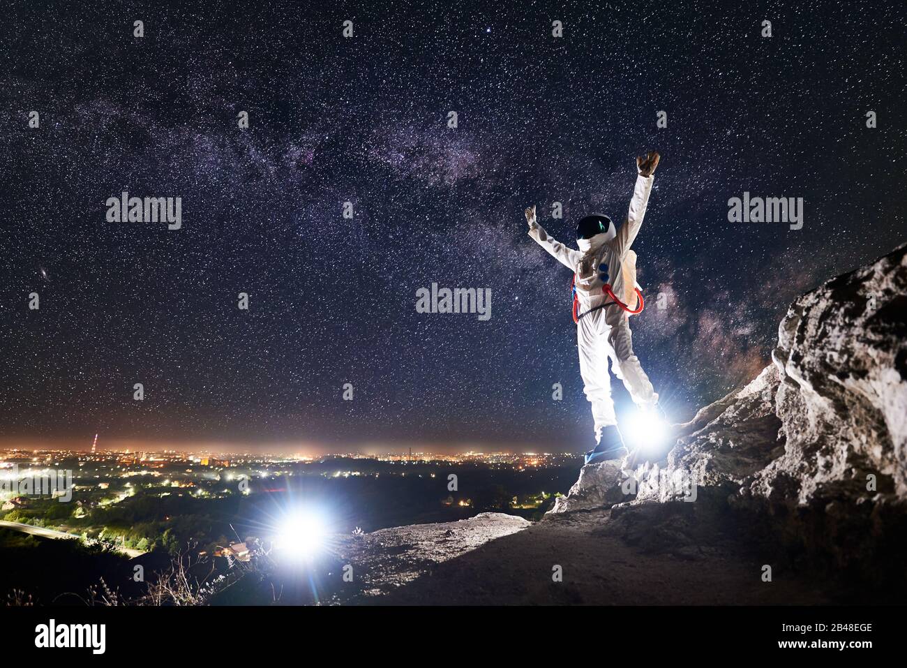 Spaceman raising arms while standing on rocky mountain with fantastic ...