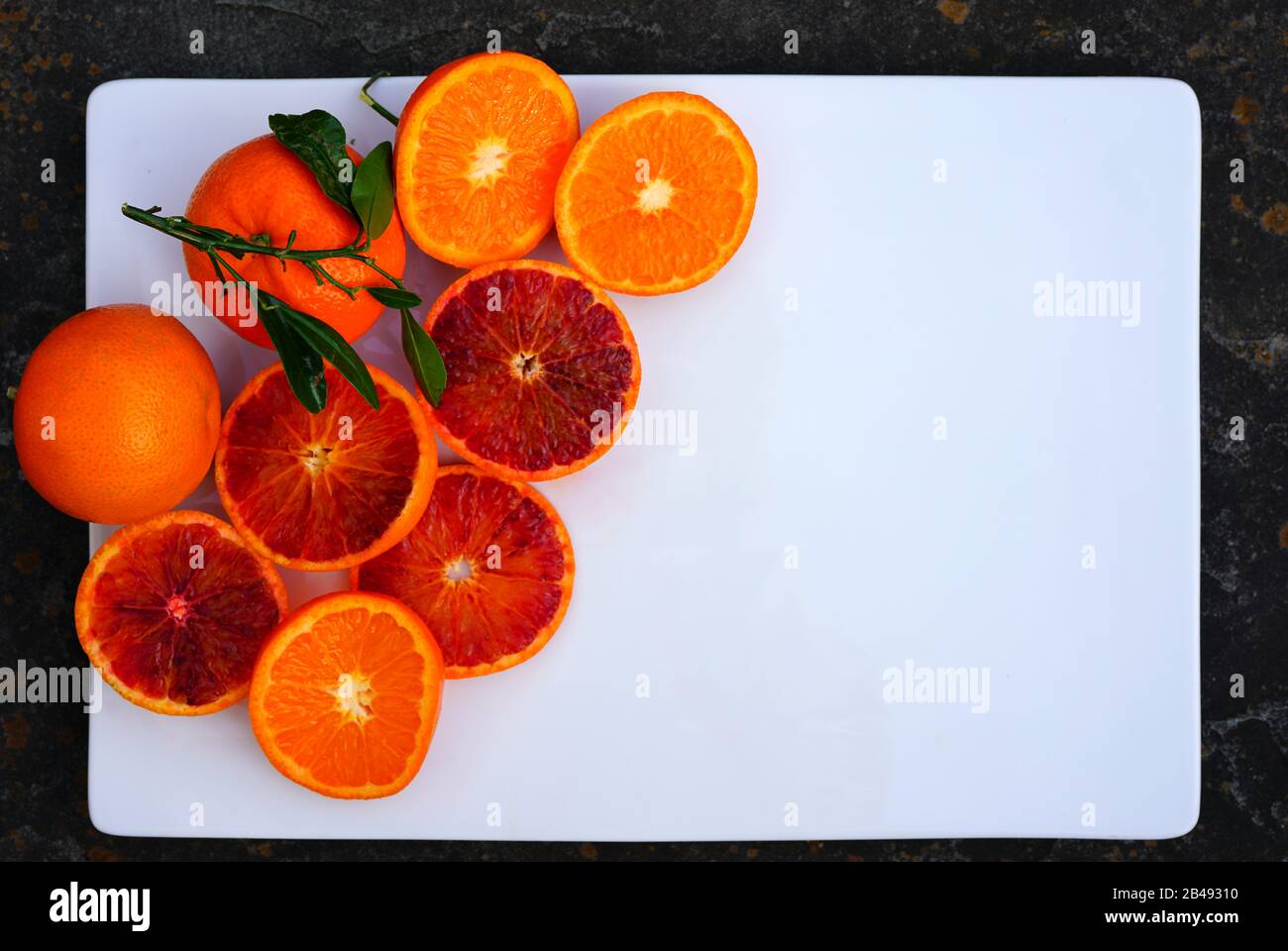 Platter of orange and mandarosa red clementines cut in half on a white ...