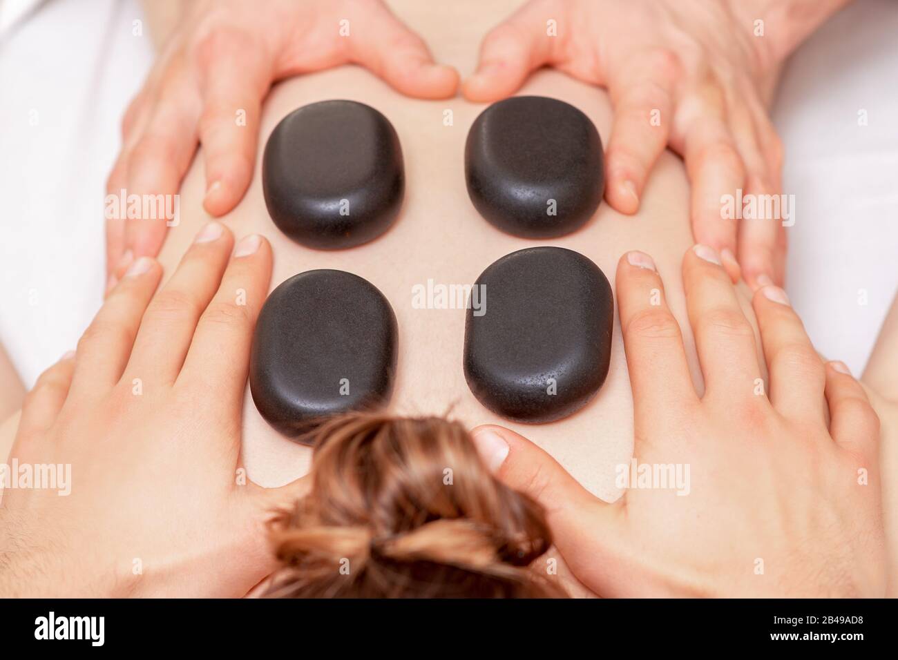 Massage stones on back of woman during back massage in four hands in ...
