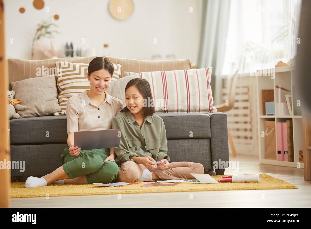 Two Asian girls sitting together on floor against sofa looking at ...