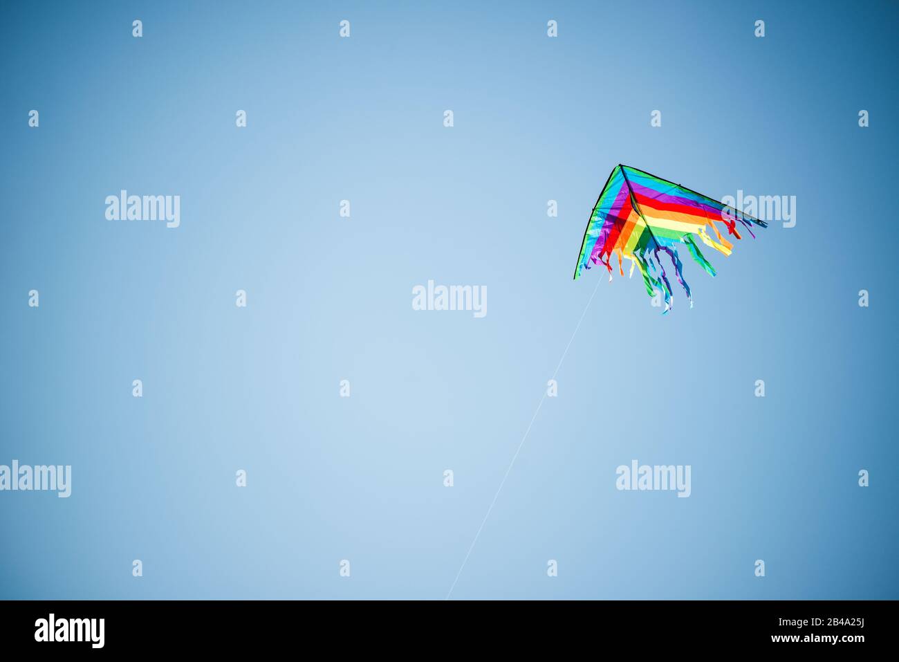 Beautiful kite in bright colors of the rainbow flies against a sunny ...