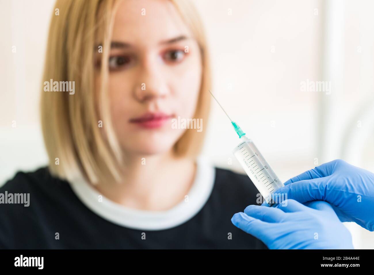 Fear of injections. Frightened girl looks at syringe needle during ...