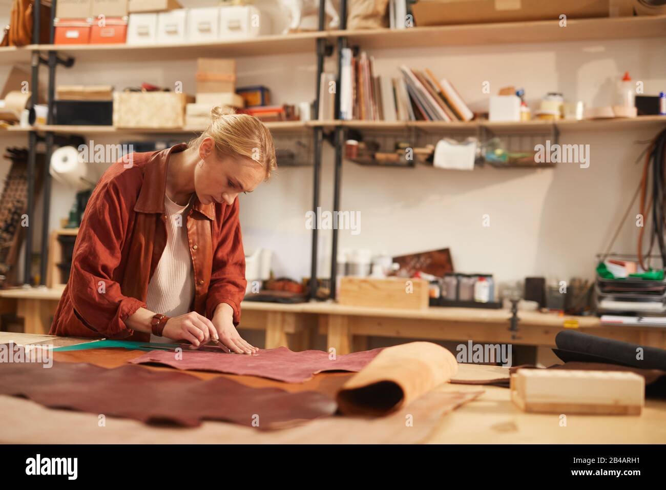 Horizontal shot of young Caucasian woman cutting out leather material ...