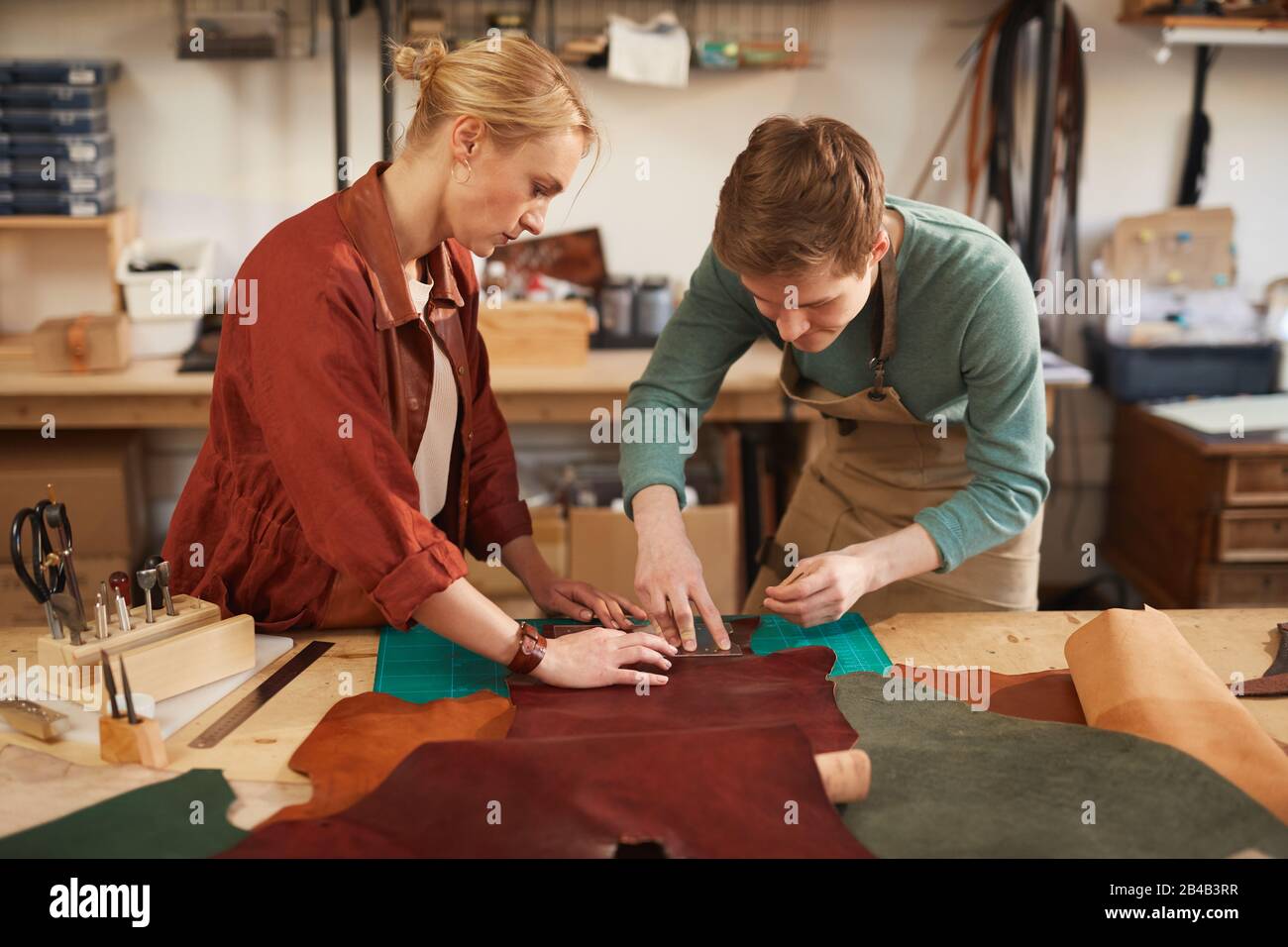 Young man creating stitching holes in leather material while woman ...