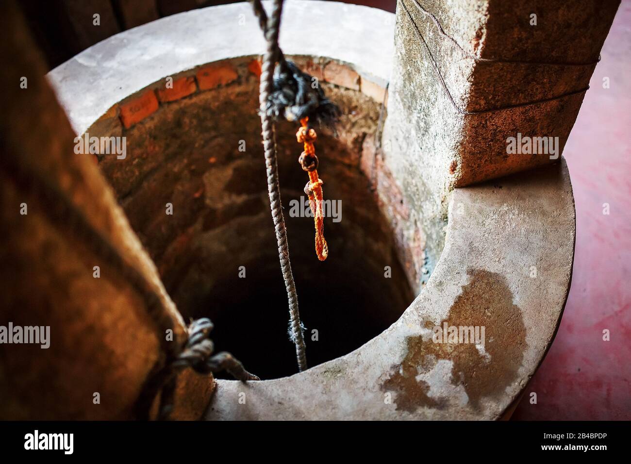 Ancient stone round well with drinking water and an orange rope. Snake ...