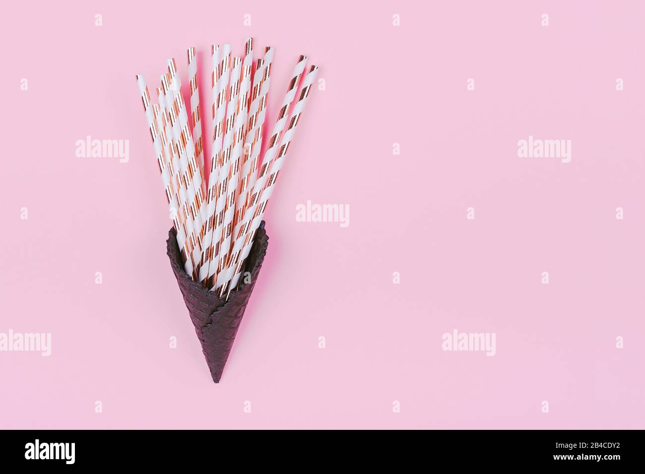 Cocktail straws with golden stripes in black ice-cream horn on pastel ...