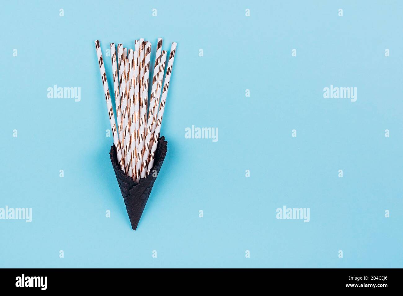 Cocktail straws with golden stripes in black ice-cream horn on pastel ...
