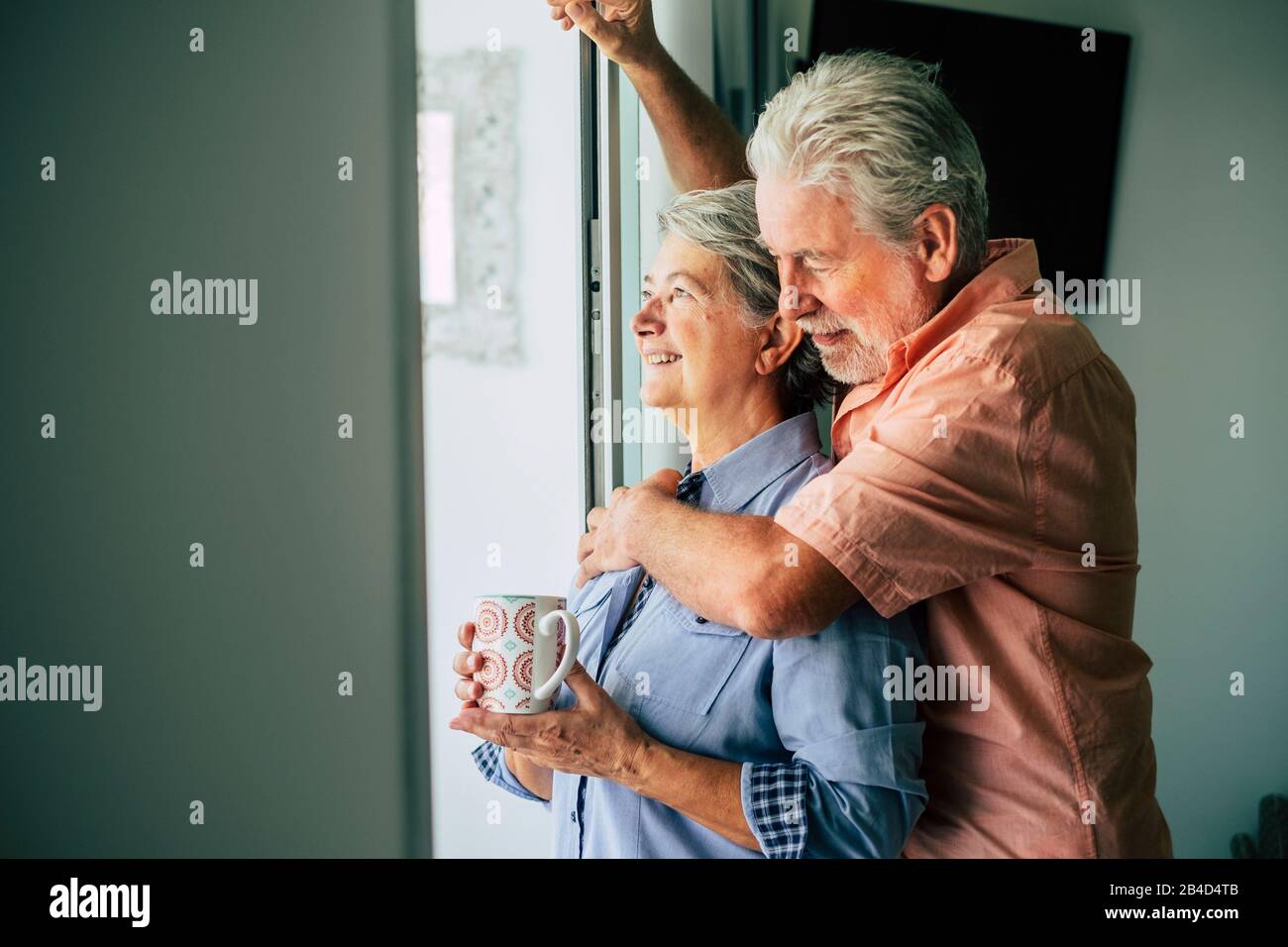 Senior couple at the window, happy, hug Stock Photo - Alamy