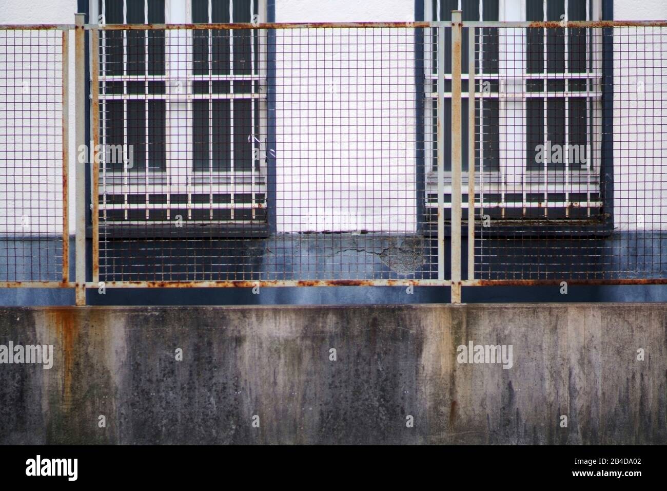 The detail of a corroding and rusting fence in front of a worn facade ...