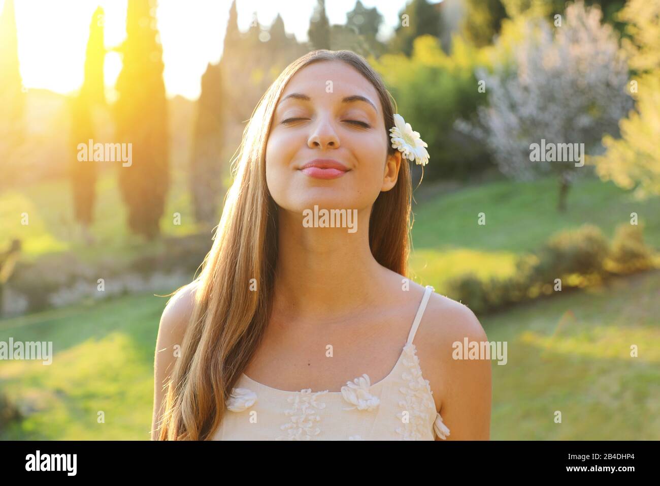 Portrait of young smiling woman with closed eyes and flower on ear ...