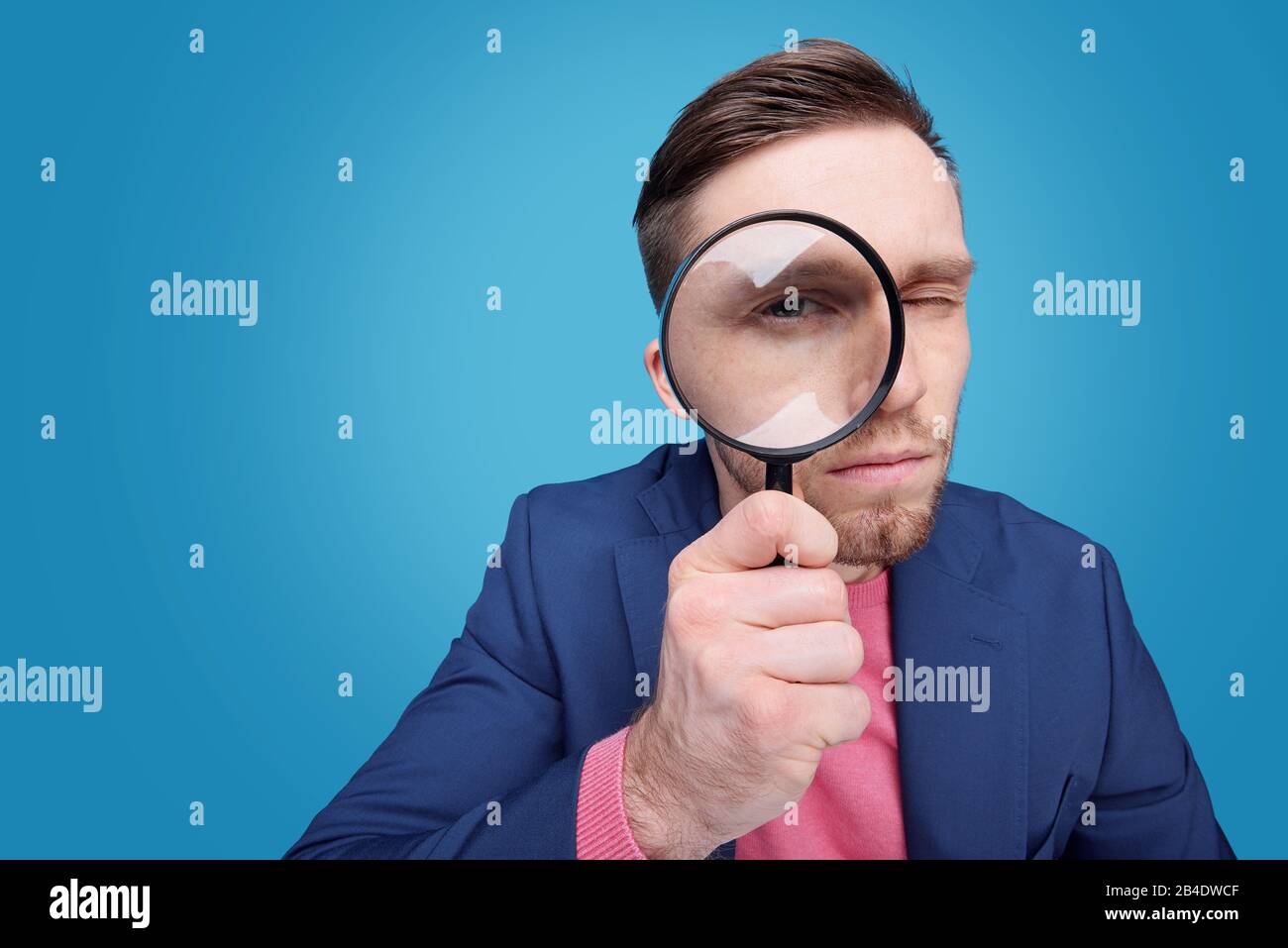 Serious young male detective holding magnifying glass by right eye ...