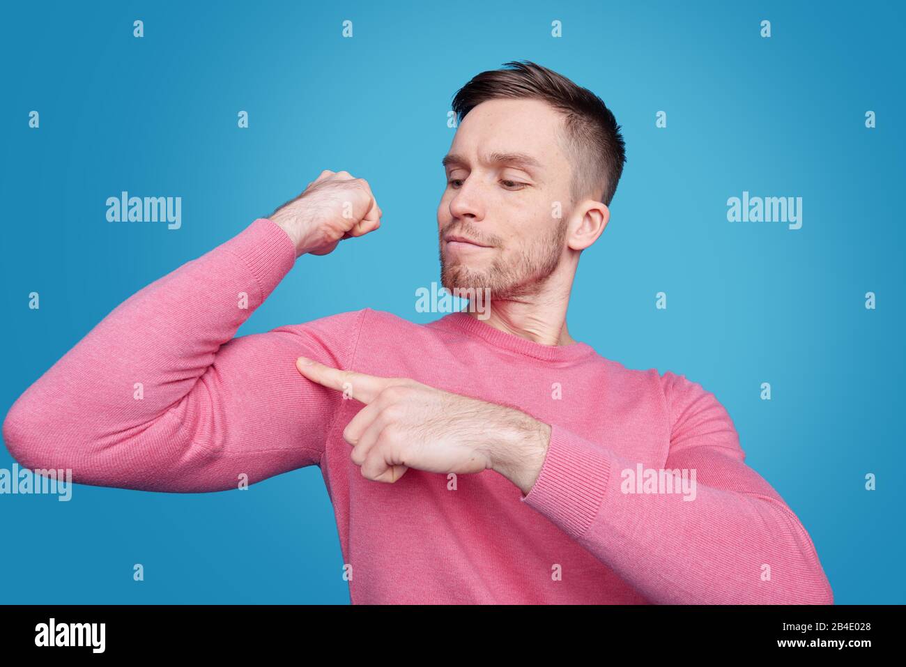 Successful young sporty man in casualwear pointing at his muscle on ...